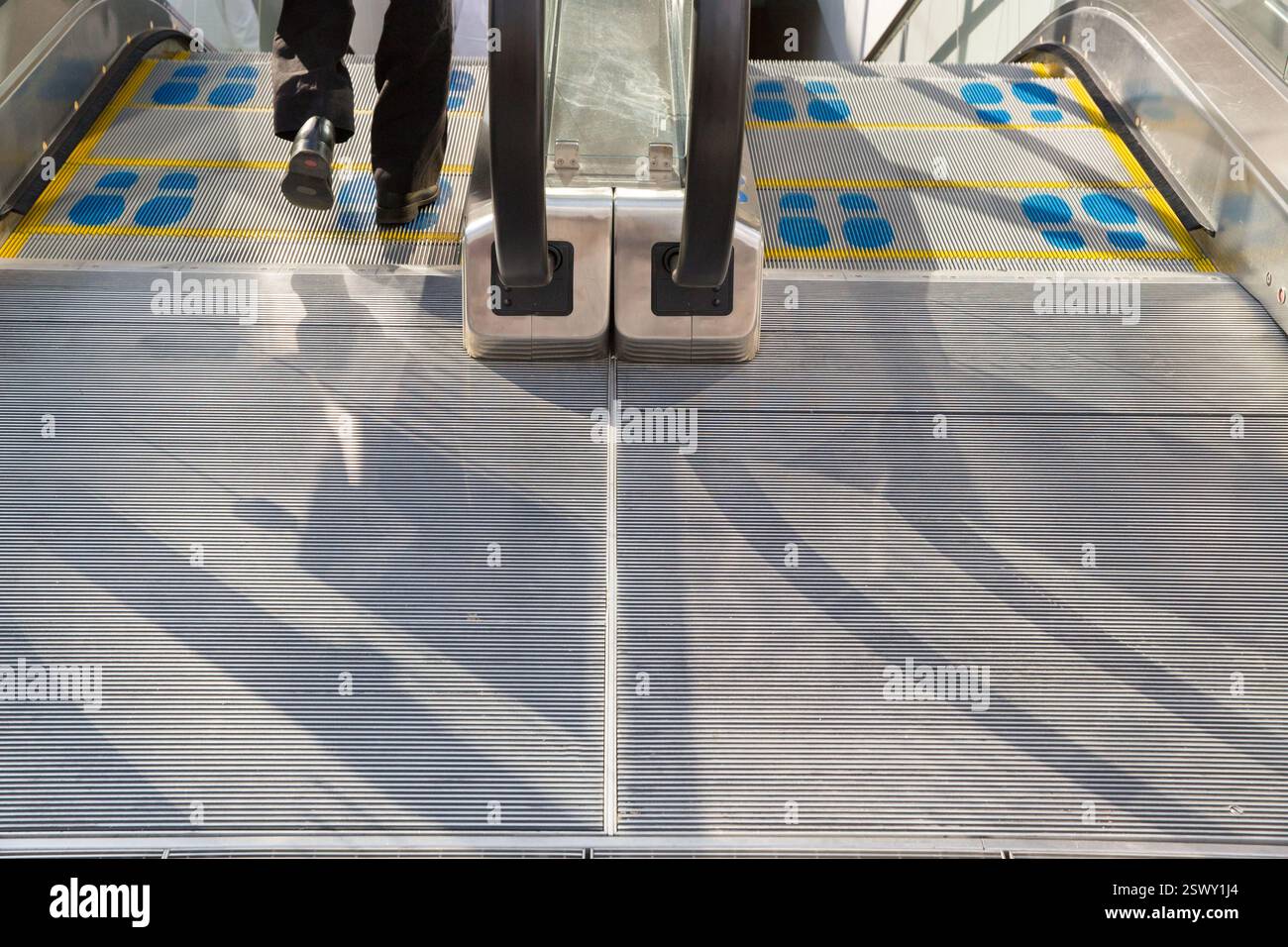 Person ascending escalator. Blue/yellow markings show proper pedestrian ...