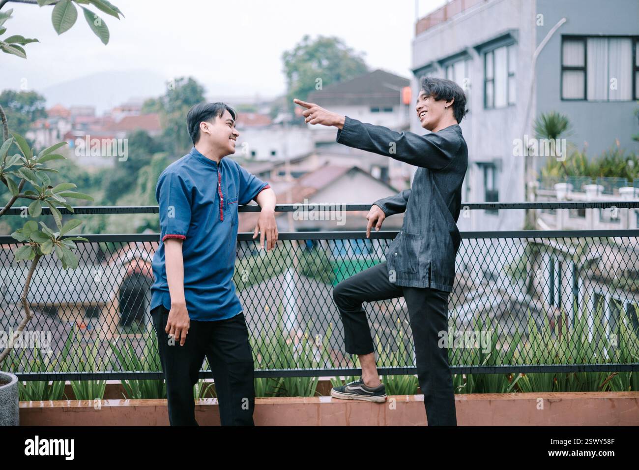 Two young men are engaged in a cheerful interaction on a rooftop ...