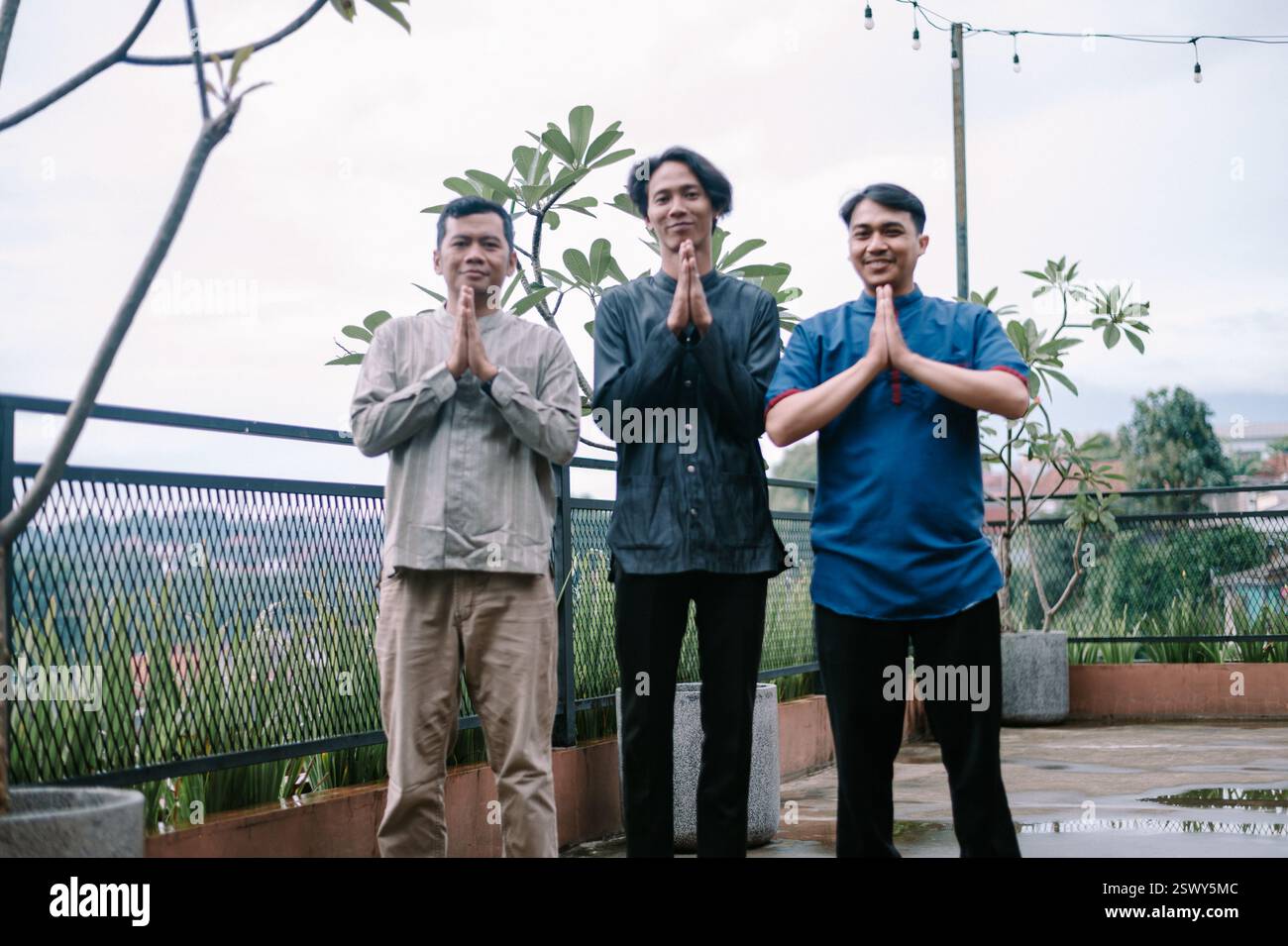 Three men stand on a rooftop, hands pressed together in a greeting ...