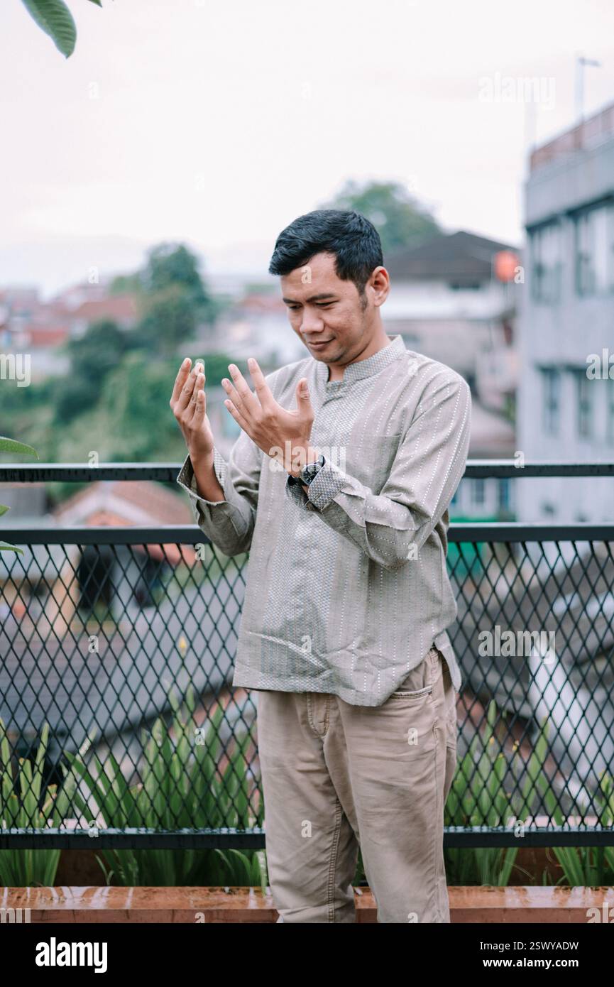 A young Muslim man stands outdoors, sincerely engaged in prayer. His ...