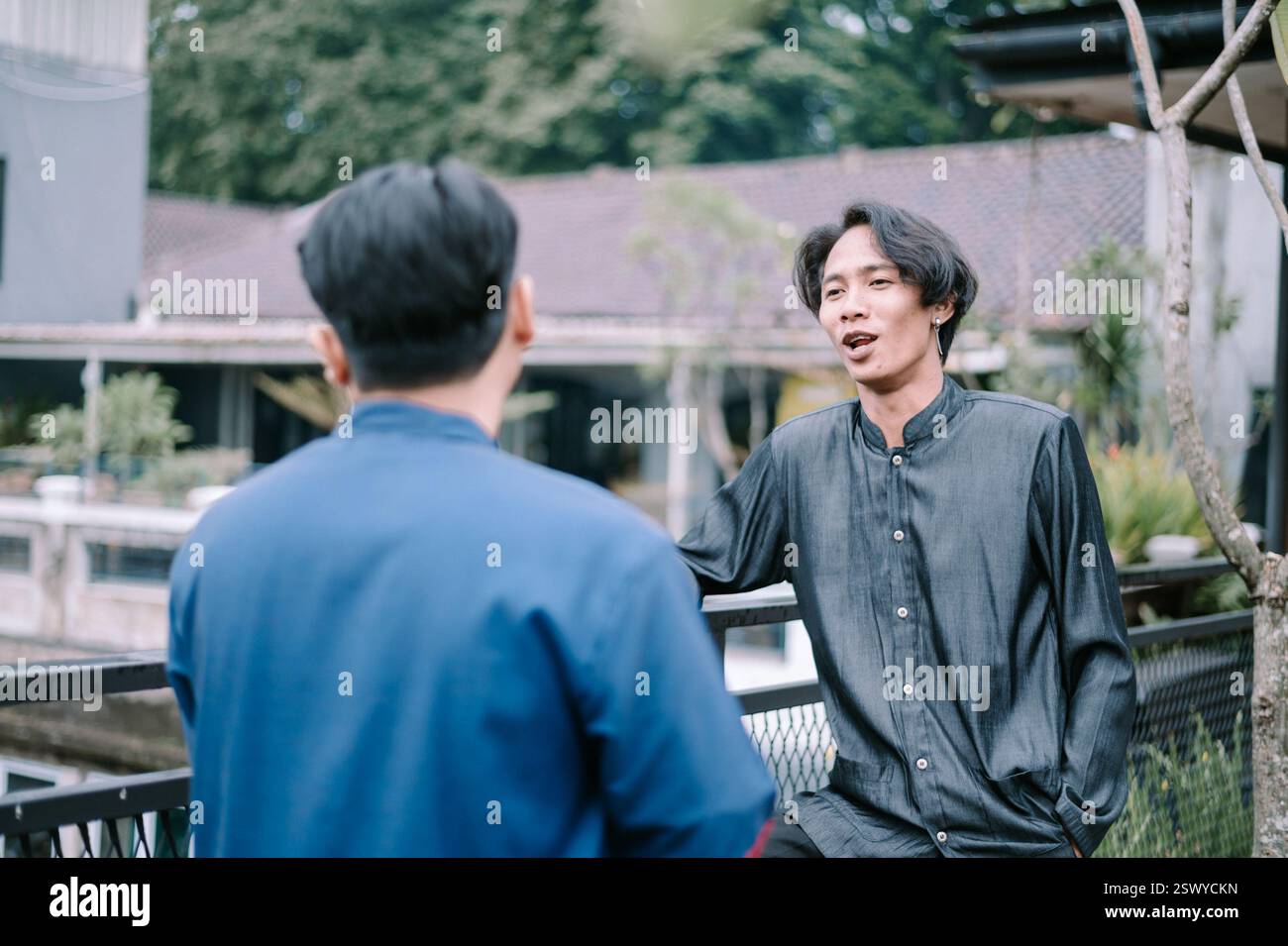Two young men are seen engaged in conversation outdoors. The ...