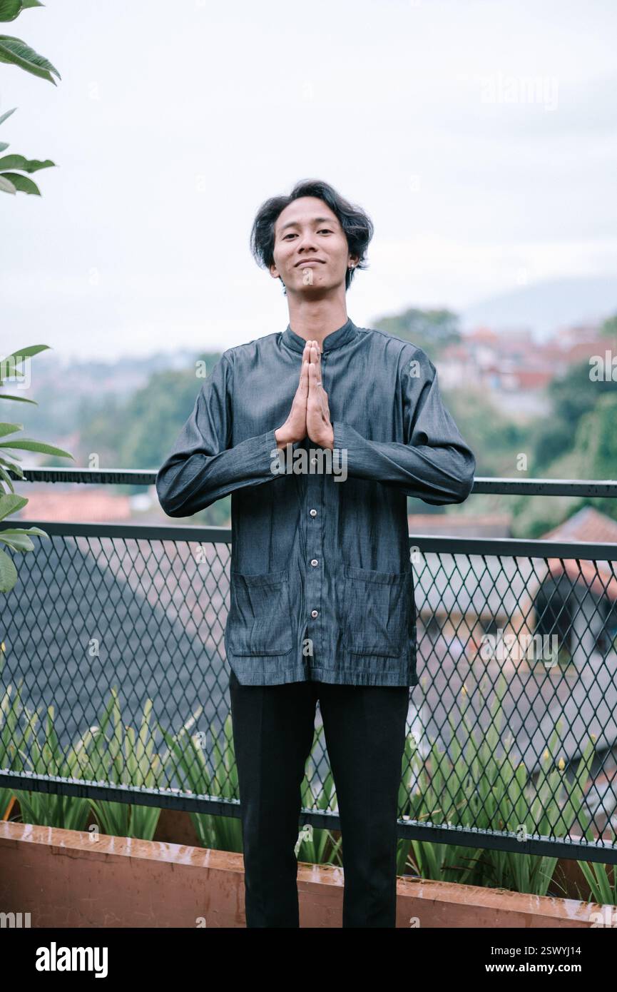 A young man with an asian appearance standing in a meditative namaste ...