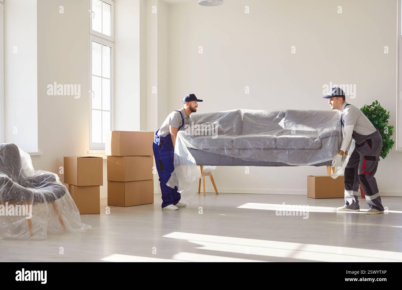 Two young moving service employees workers carrying heavy sofa together ...