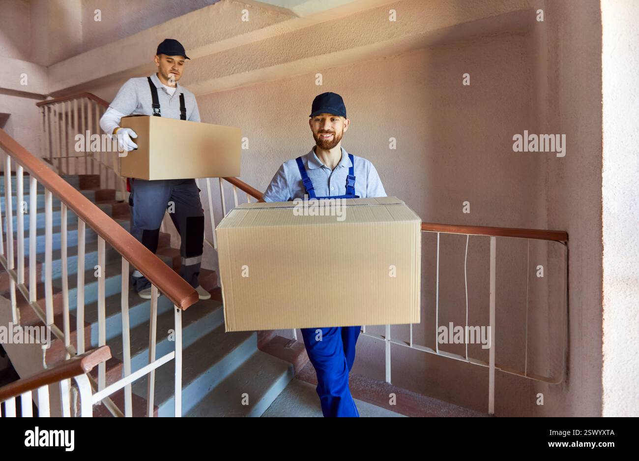 Professional movers carrying cardboard boxes down stairs, providing ...