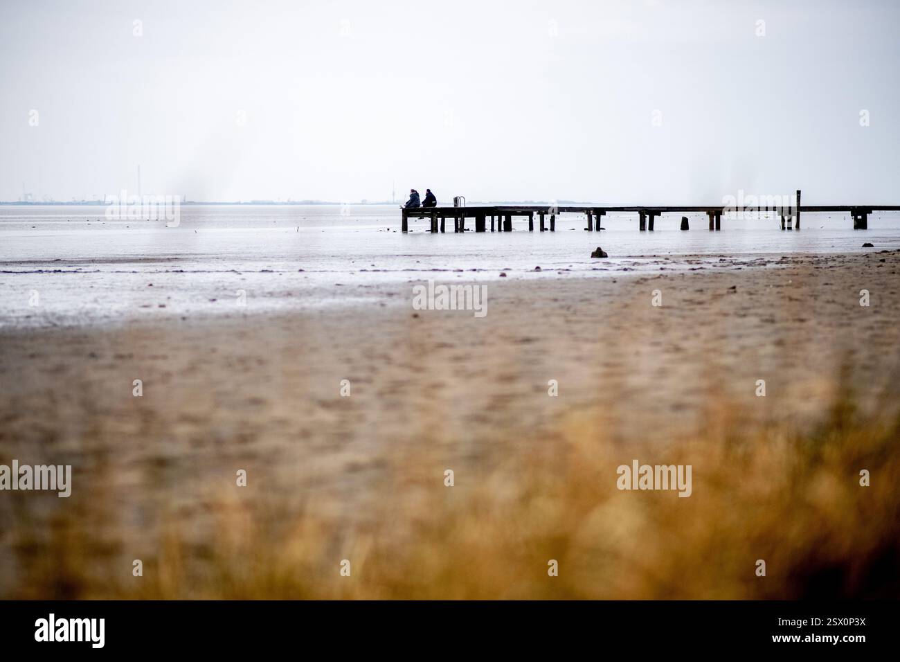 Dangast, Germany. 22nd Feb, 2025. Two people sit on a wooden jetty on ...
