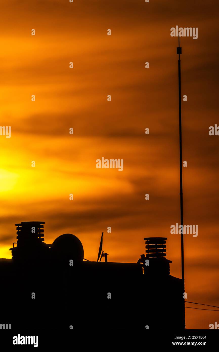 A silhouette of a rooftop with chimneys and antennas contrasts against ...