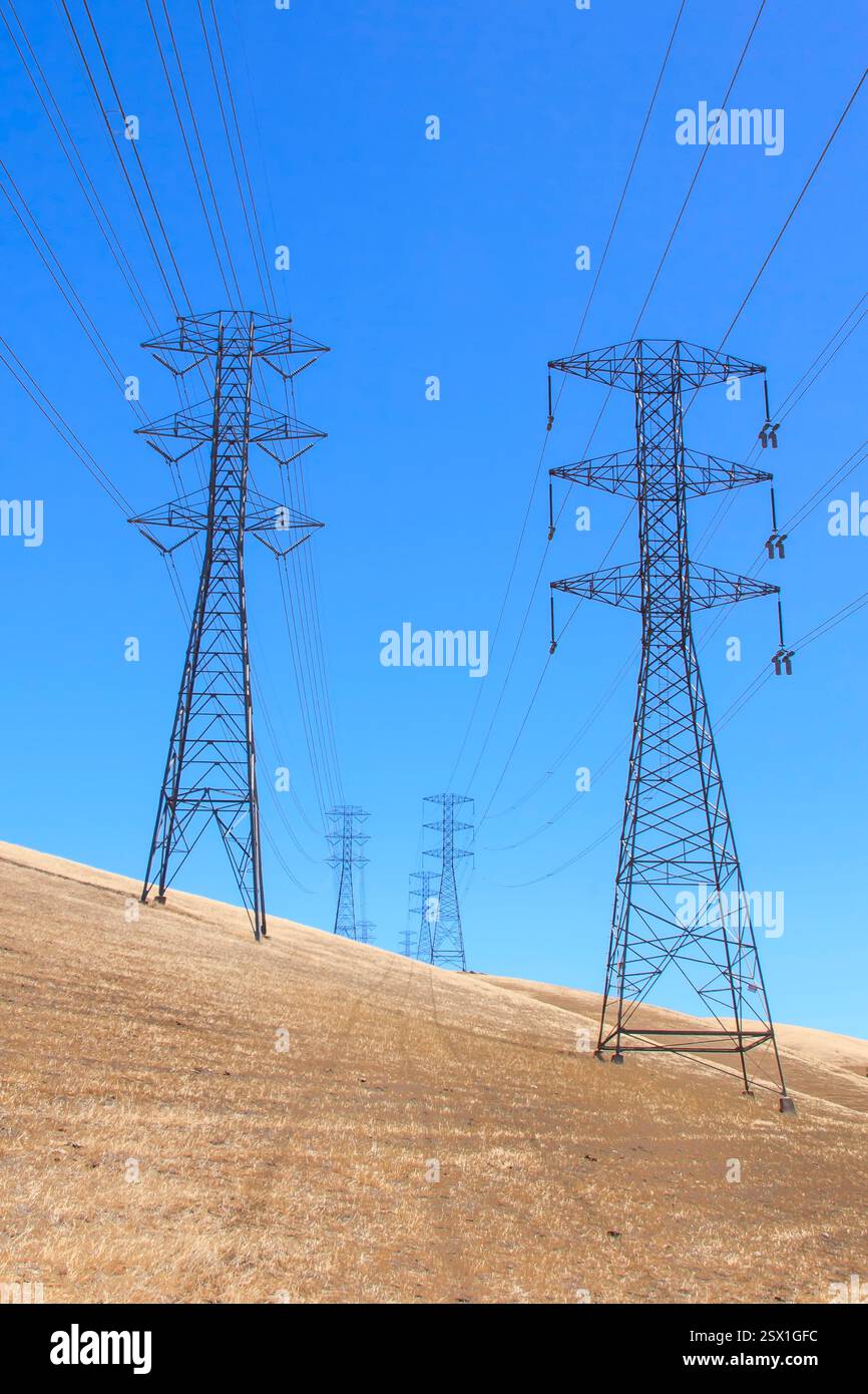 Three tall power lines are on a hill. The wires are connected to a ...