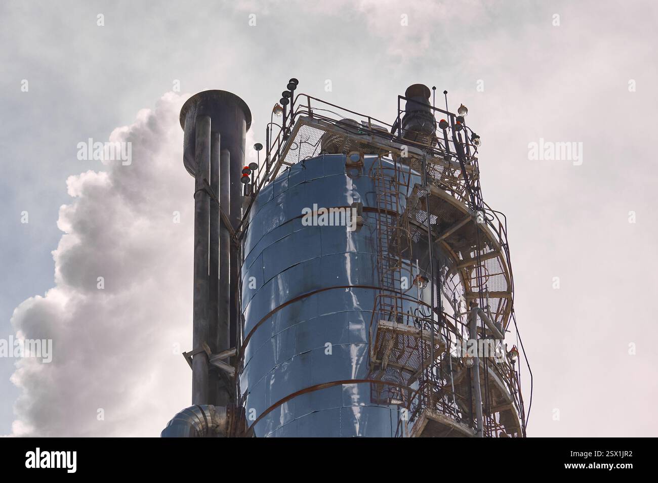 Distillation column towering above a chemical plant under a cloudy sky ...