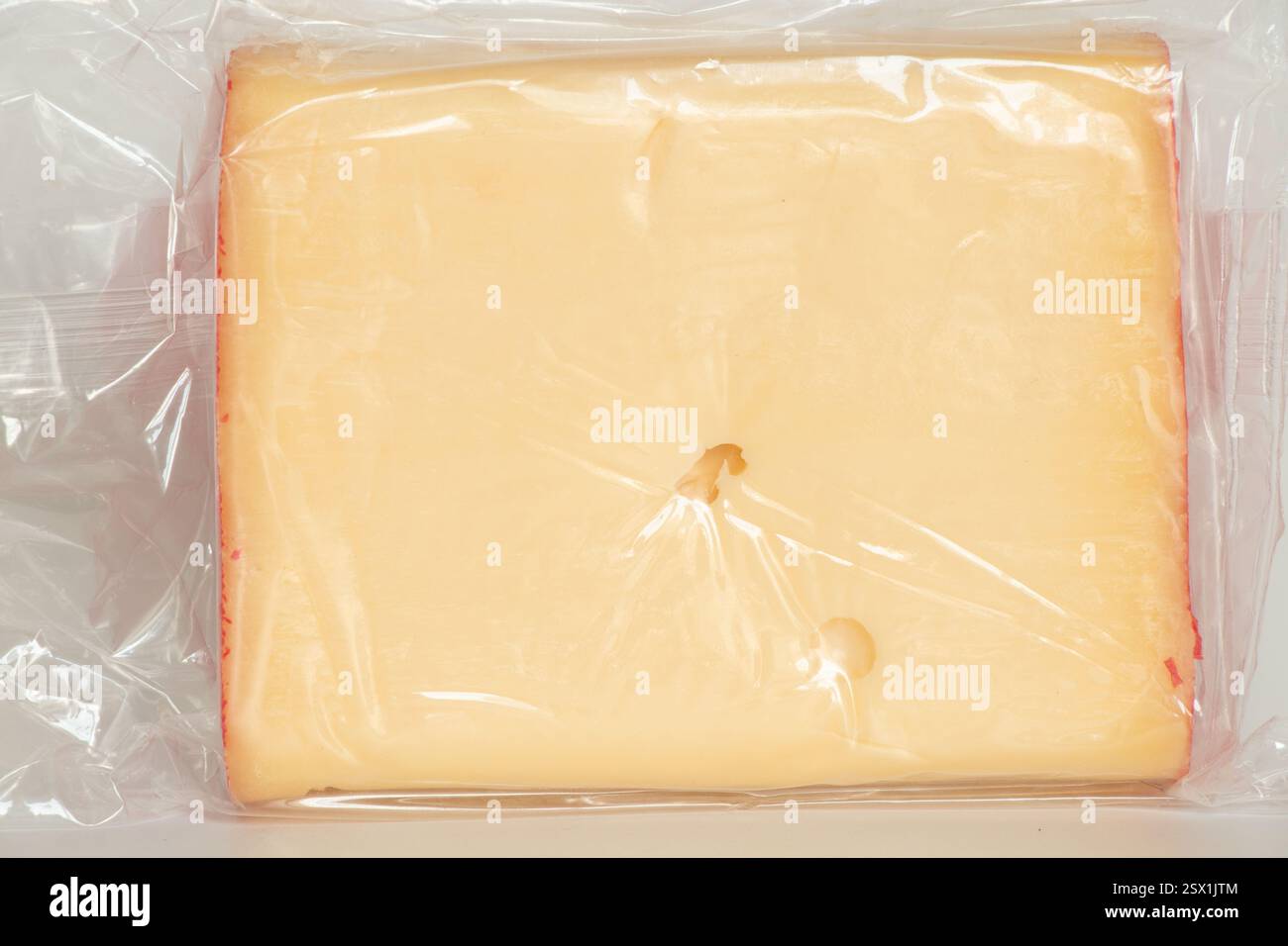 Piece of hard cheese in packaging on white background close-up ...