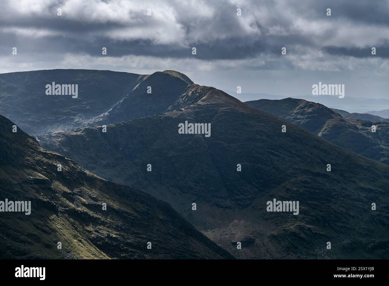 Lush green mountains stretch across the horizon, shrouded in shadows ...