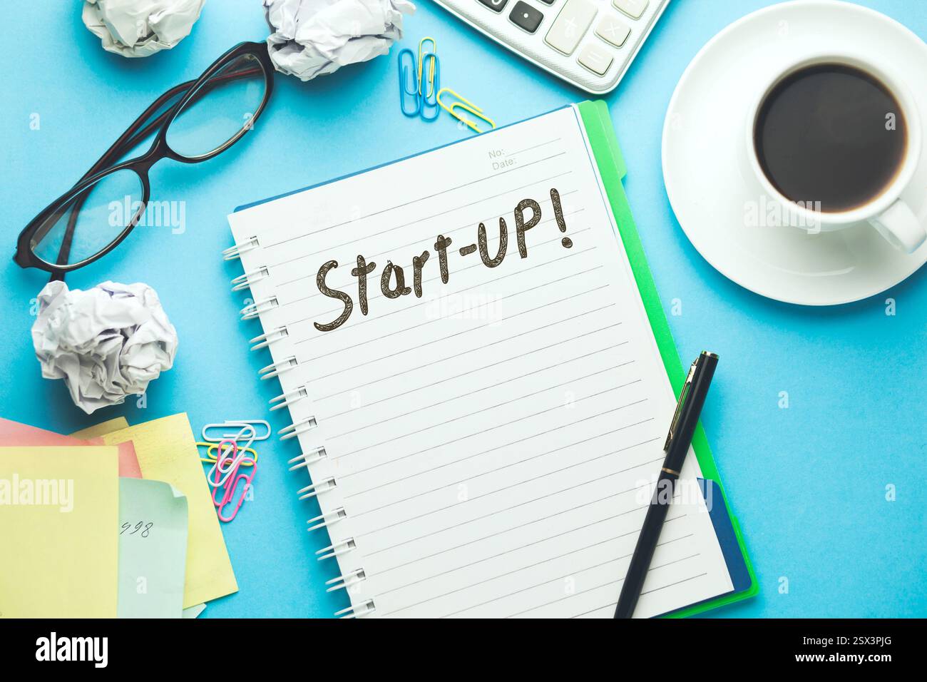 Start up word on notebook page with calculator and coffee on blue table ...