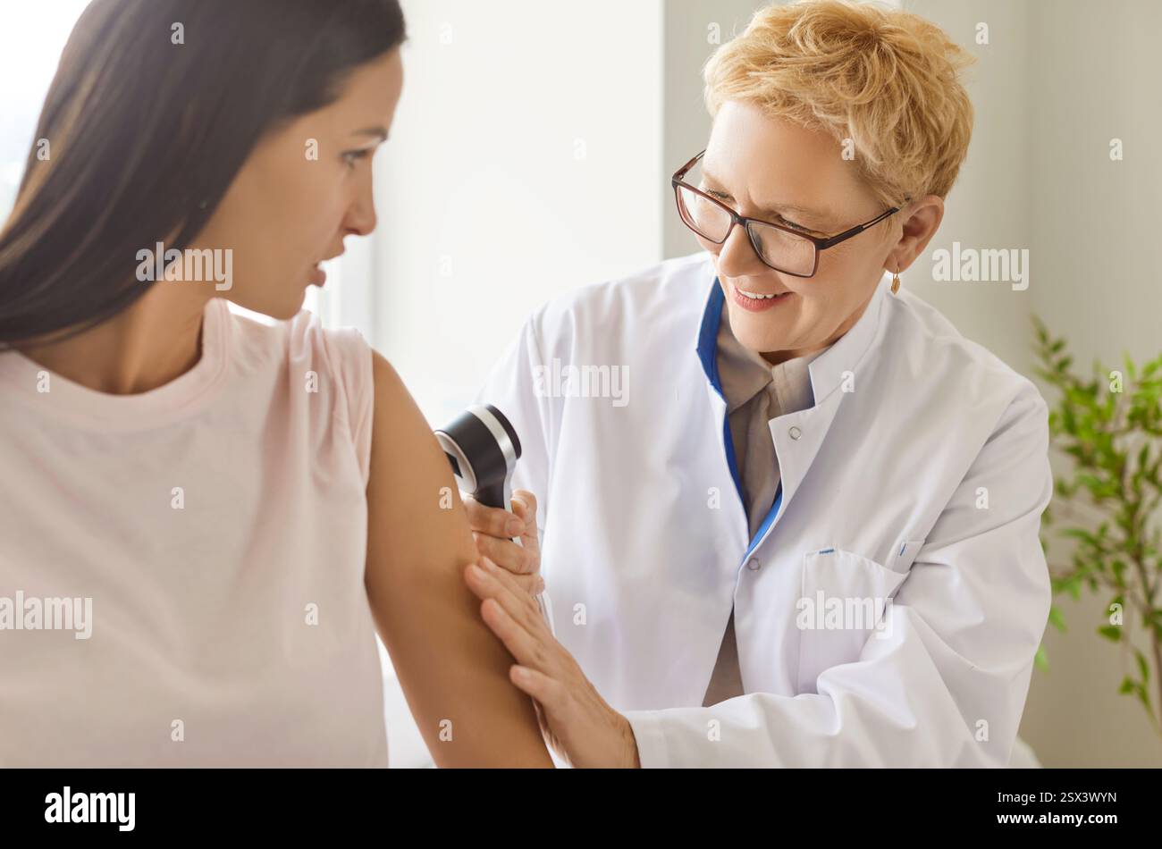Smiling female doctor dermatologist examining young woman skin with ...