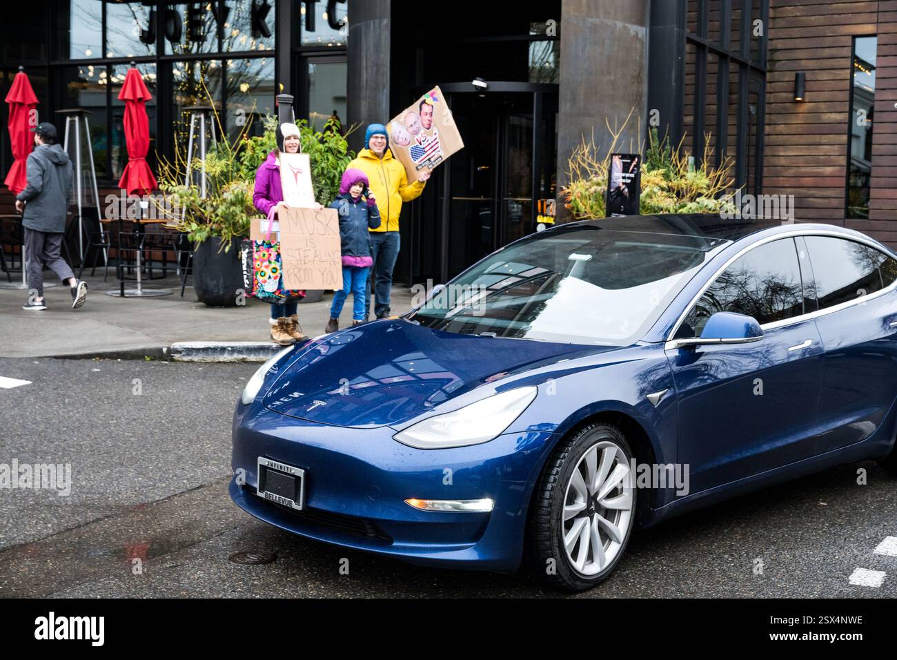 Seattle, USA. 22 Feb 2025. A Tesla passes by activists at the Tesla ...
