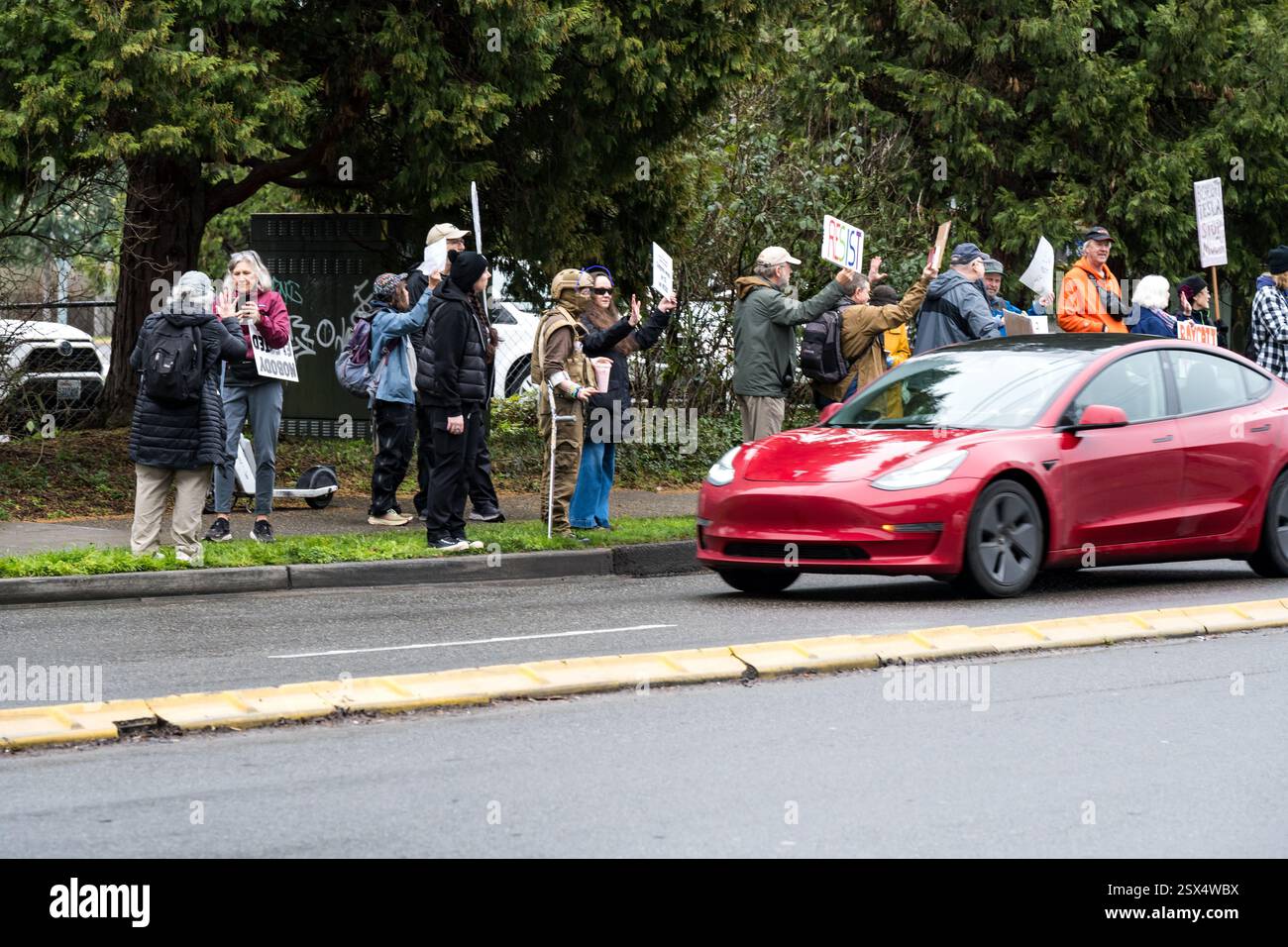 Seattle, USA. 22 Feb 2025. A Tesla passes by activists at the Tesla ...