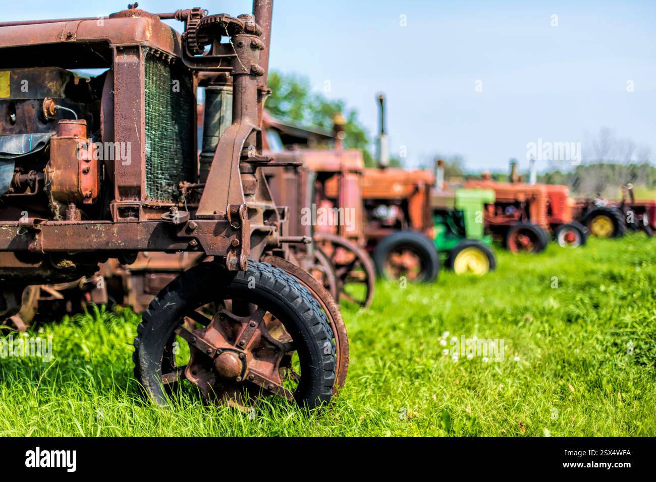 Row of old tractors are parked in a field. The first tractor is green ...
