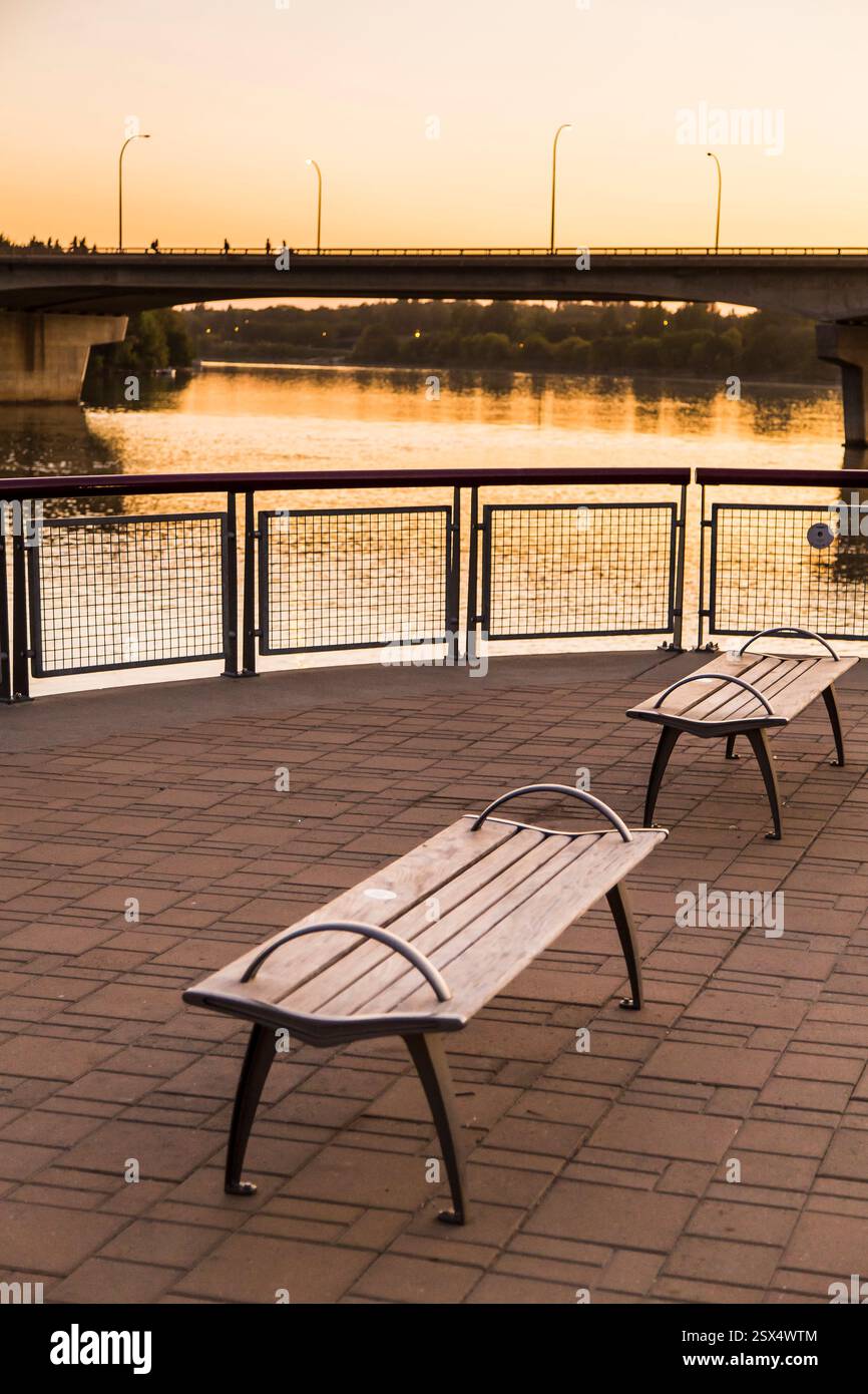 Two benches are sitting on a brick walkway next to a river. The benches ...