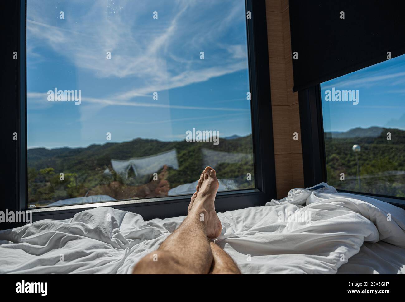 First point of view of man's feet relaxing in bed with mountain views ...