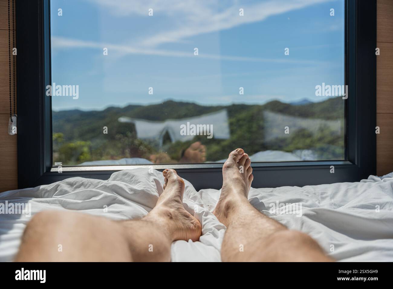 First point of view of man's feet relaxing in bed with mountain views ...