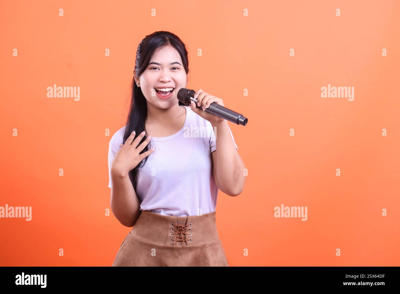 A smiling young Asian woman singing passionately into a microphone. She ...