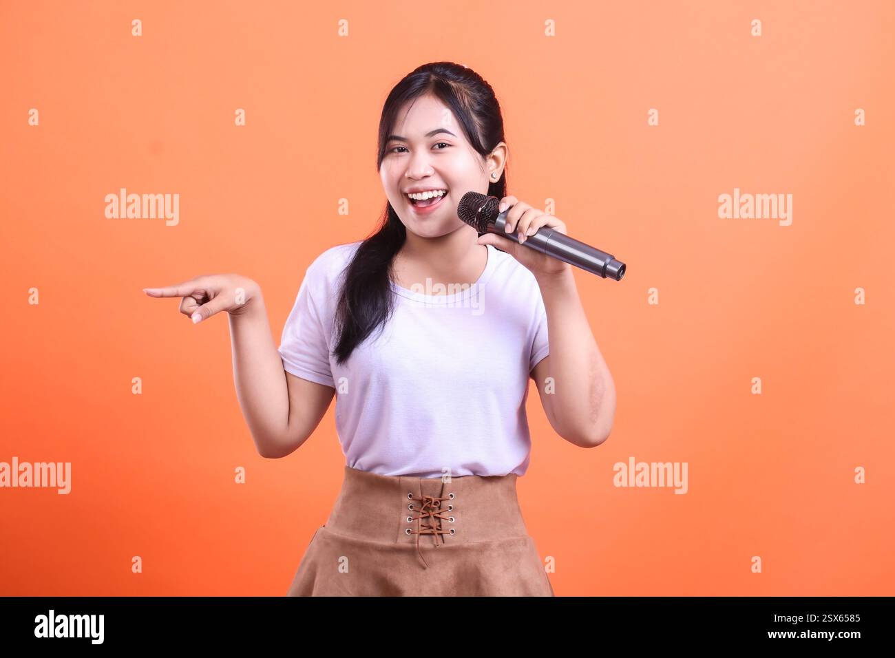 A young woman singing with a microphone and pointing with her left hand ...