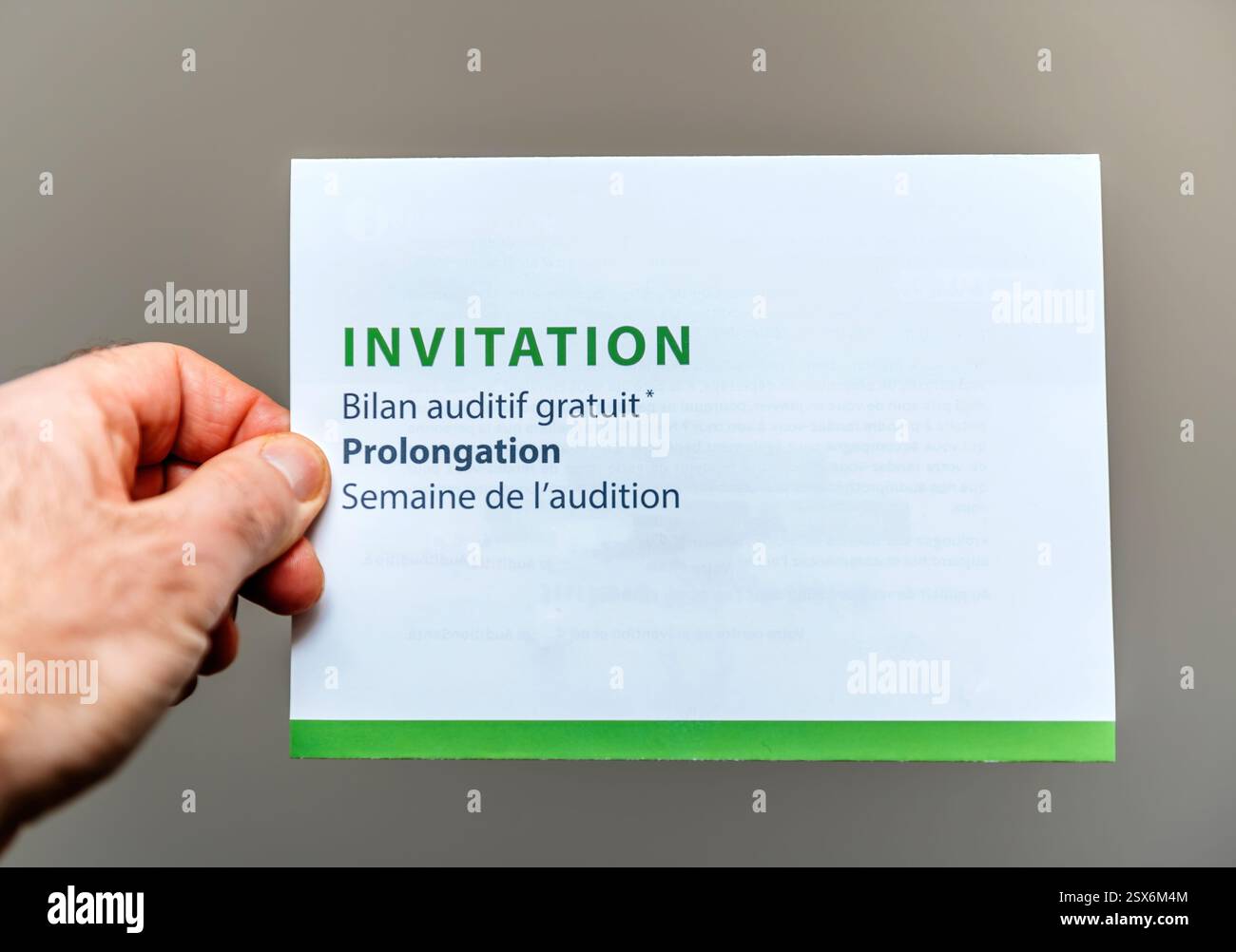 A hand holding an invitation card for a free hearing assessment during ...