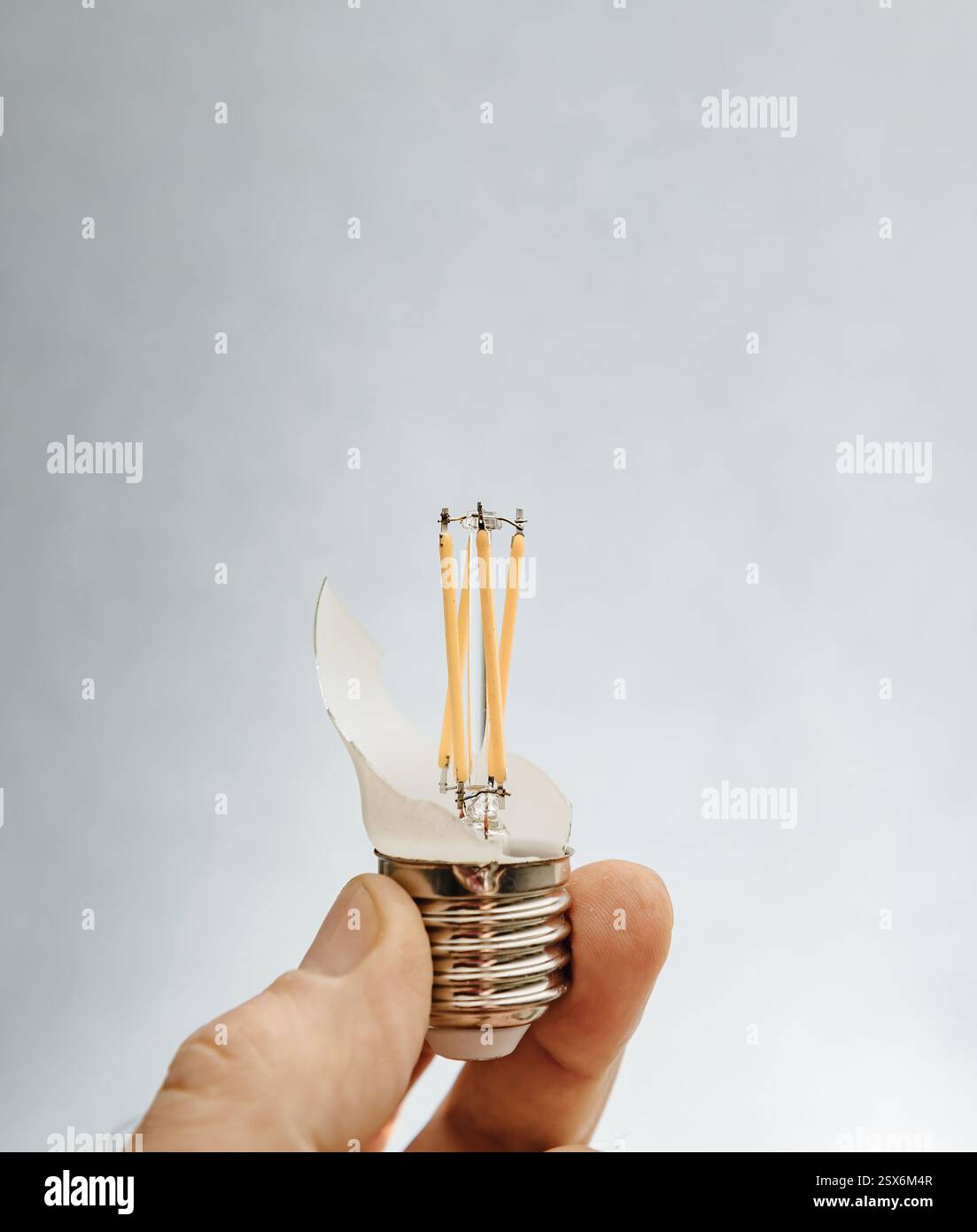 A person holds a shattered LED filament bulb, exposing internal yellow ...