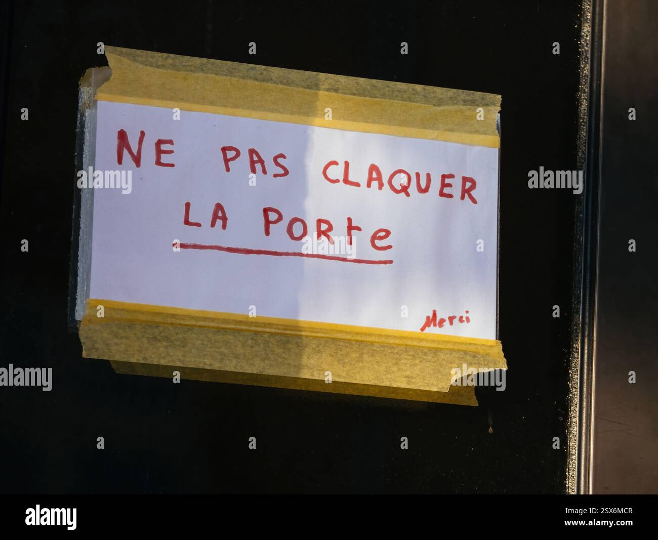 A handwritten sign taped to a black door, instructing in French not to ...