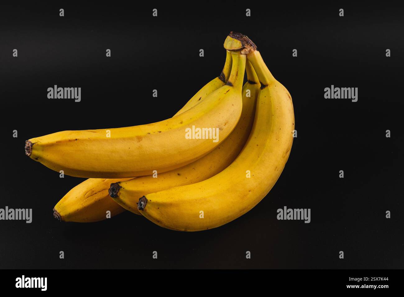 A cluster of ripe yellow bananas rests on a dark background ...