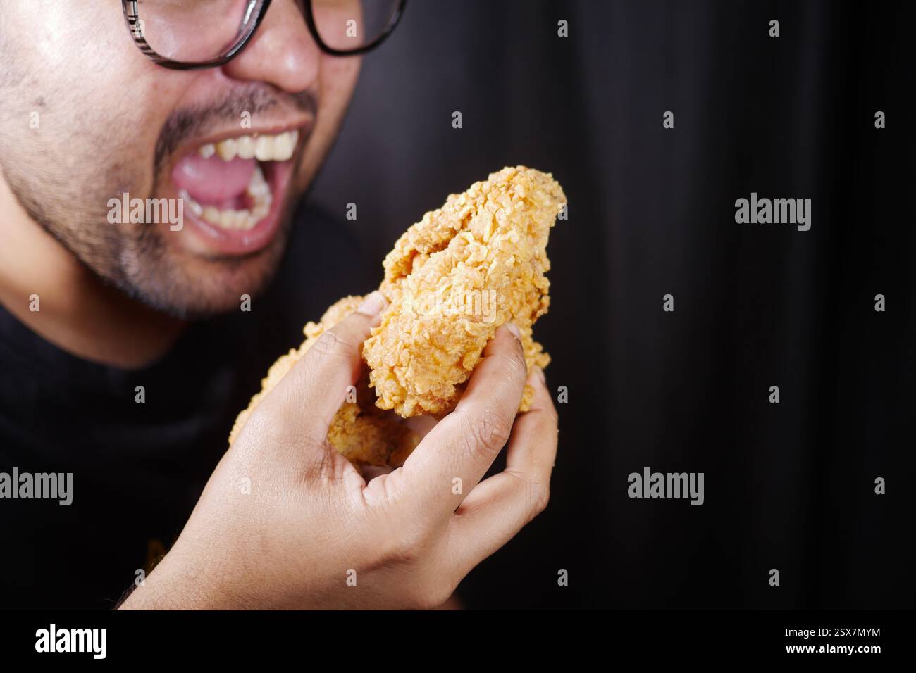 Enjoying a crispy piece of fried chicken with enthusiasm Stock Photo ...