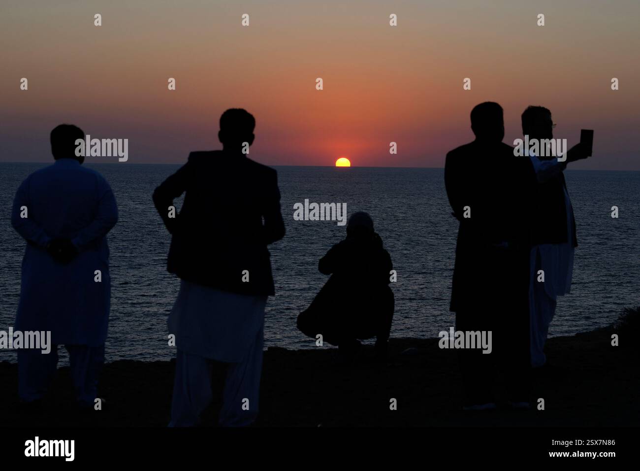 People take pictures as the sun sets along the beach in the coastal ...