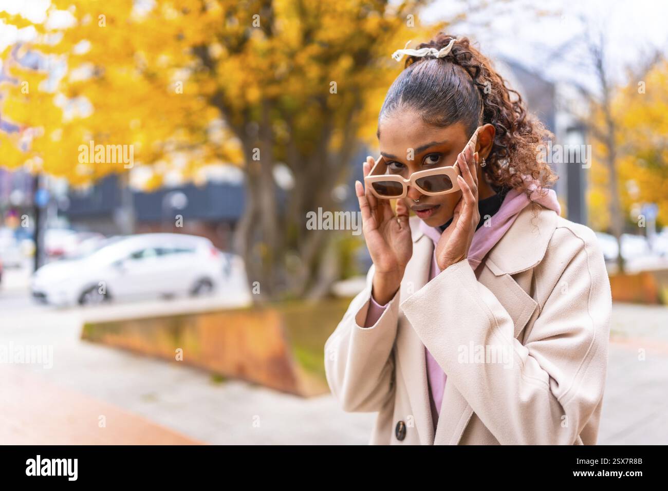 Flirty young african woman with sunglasses and coat in the city in a ...