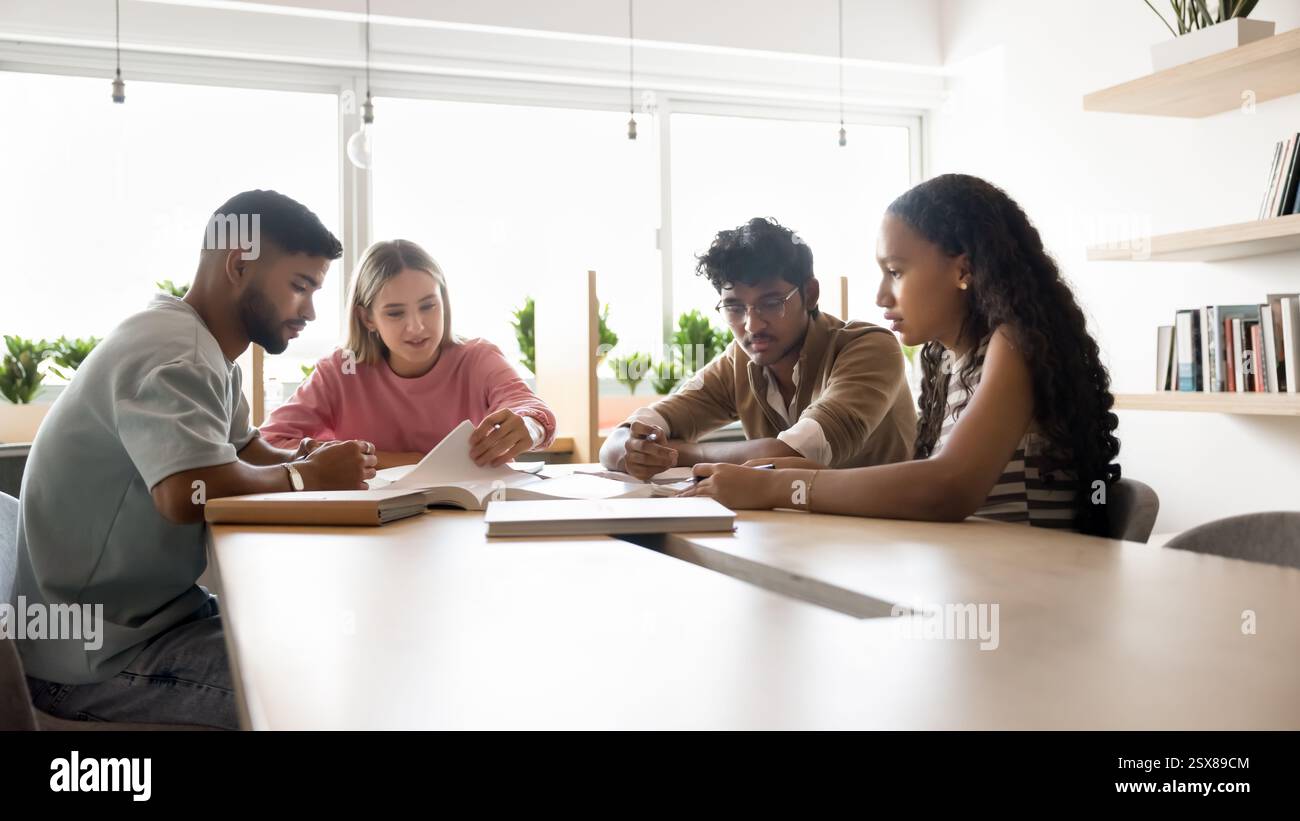 Four students gathered around table in modern study space Stock Photo ...