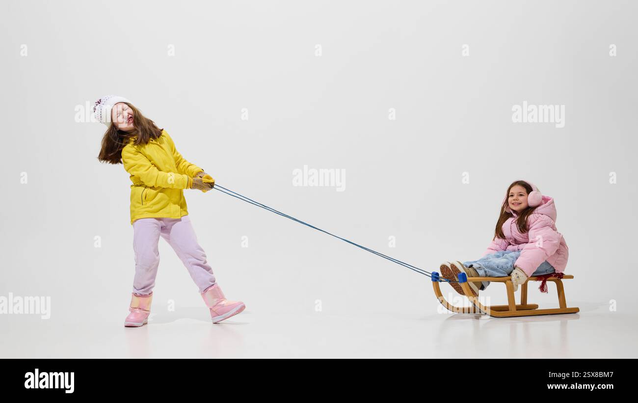 Girl pulling sled with friend, smiling, dressed in yellow winter coat ...
