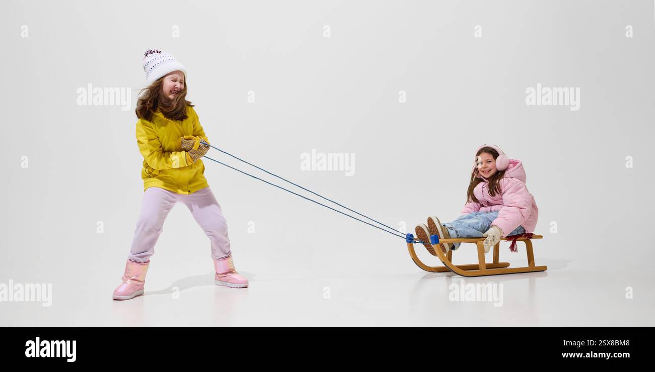 Girl pulling sled with friend, smiling, dressed in yellow winter coat ...