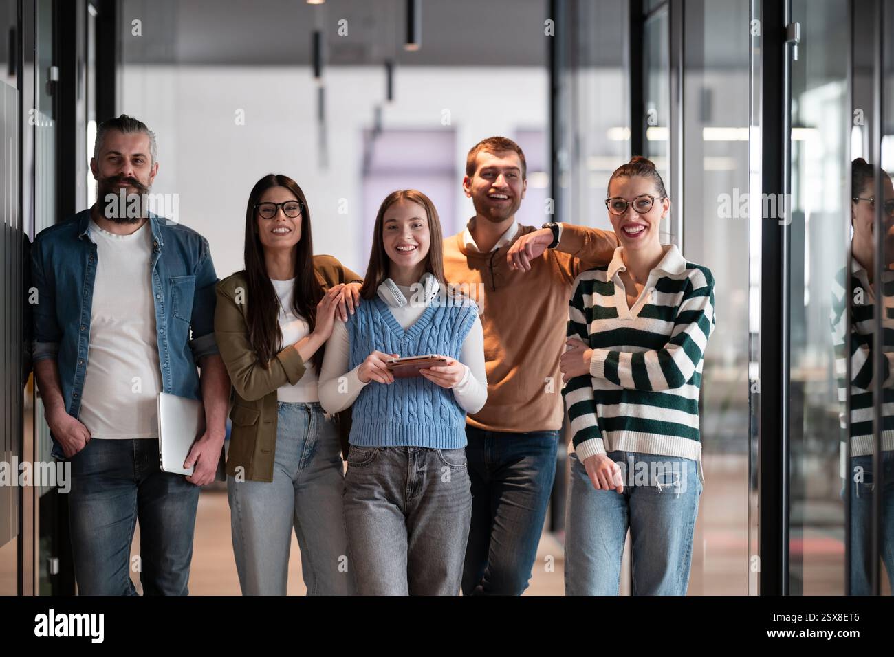 A diverse team of professionals in a modern coworking startup office smiles together, showcasing ...