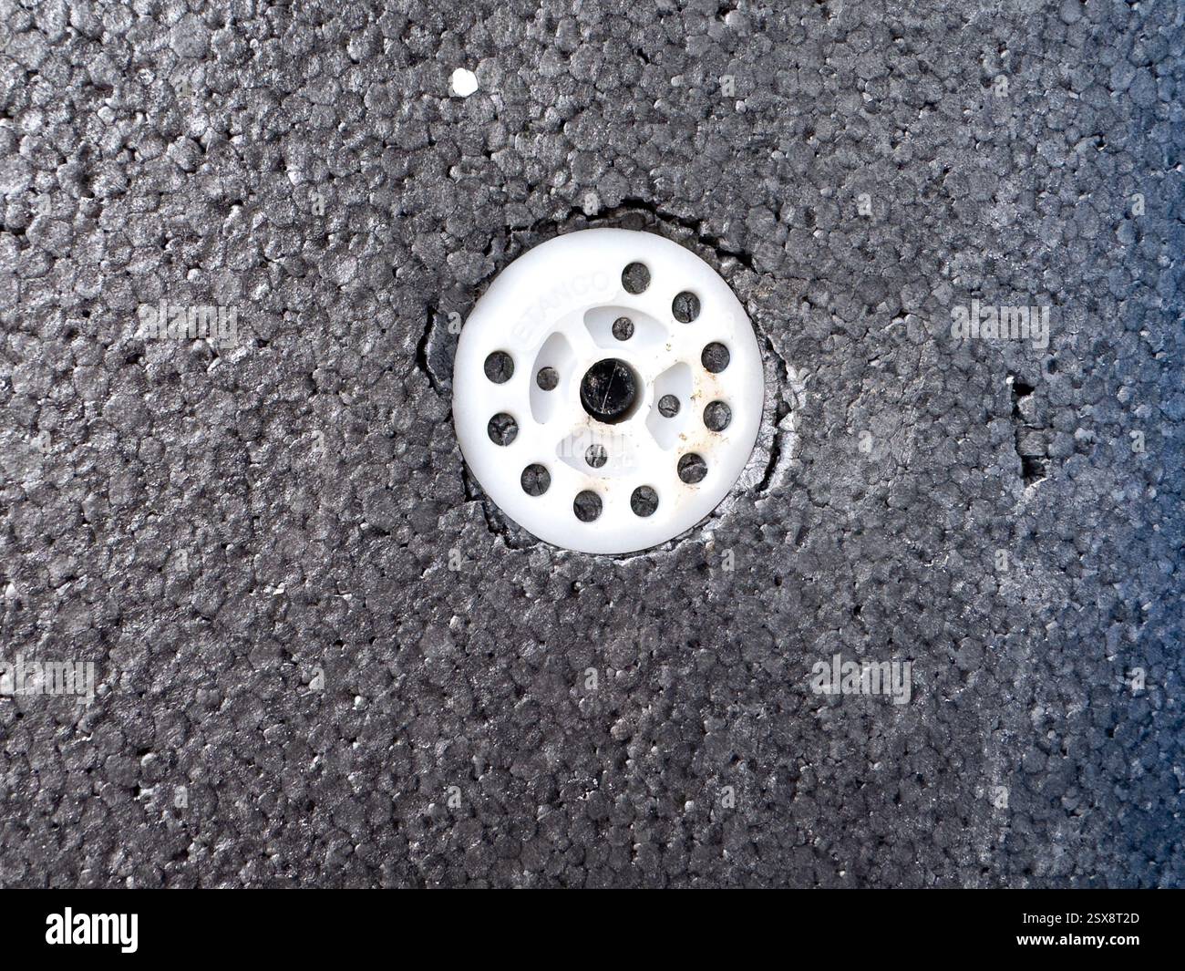 Drain cover embedded in textured black surface during bright daylight ...