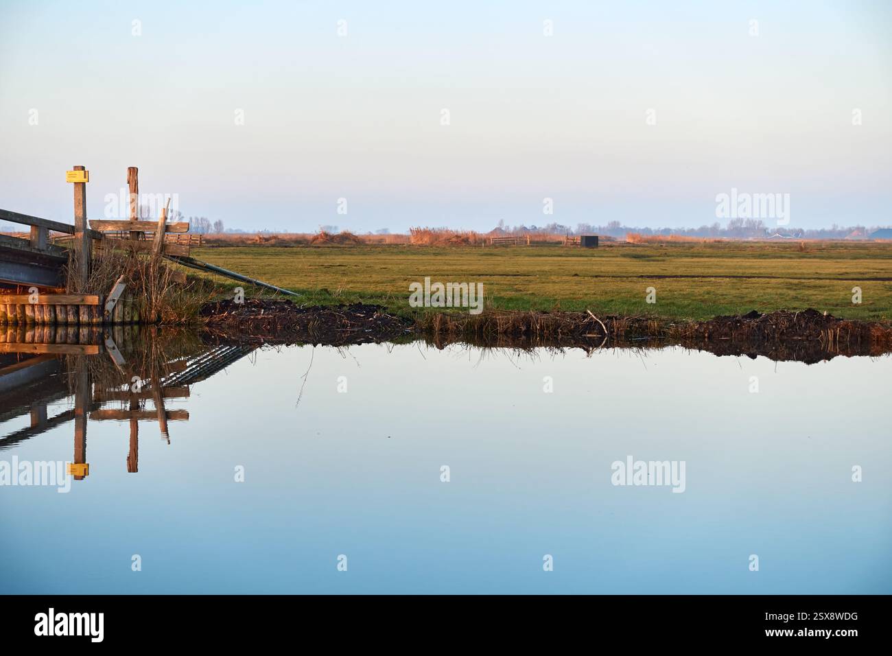 Still water reflects a wooden bridge and vast Dutch wetlands during ...