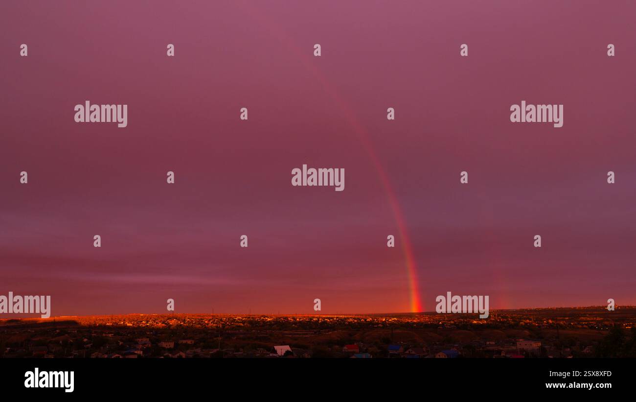 Faint rainbow arching across a dramatic sunset sky over rooftops Stock ...