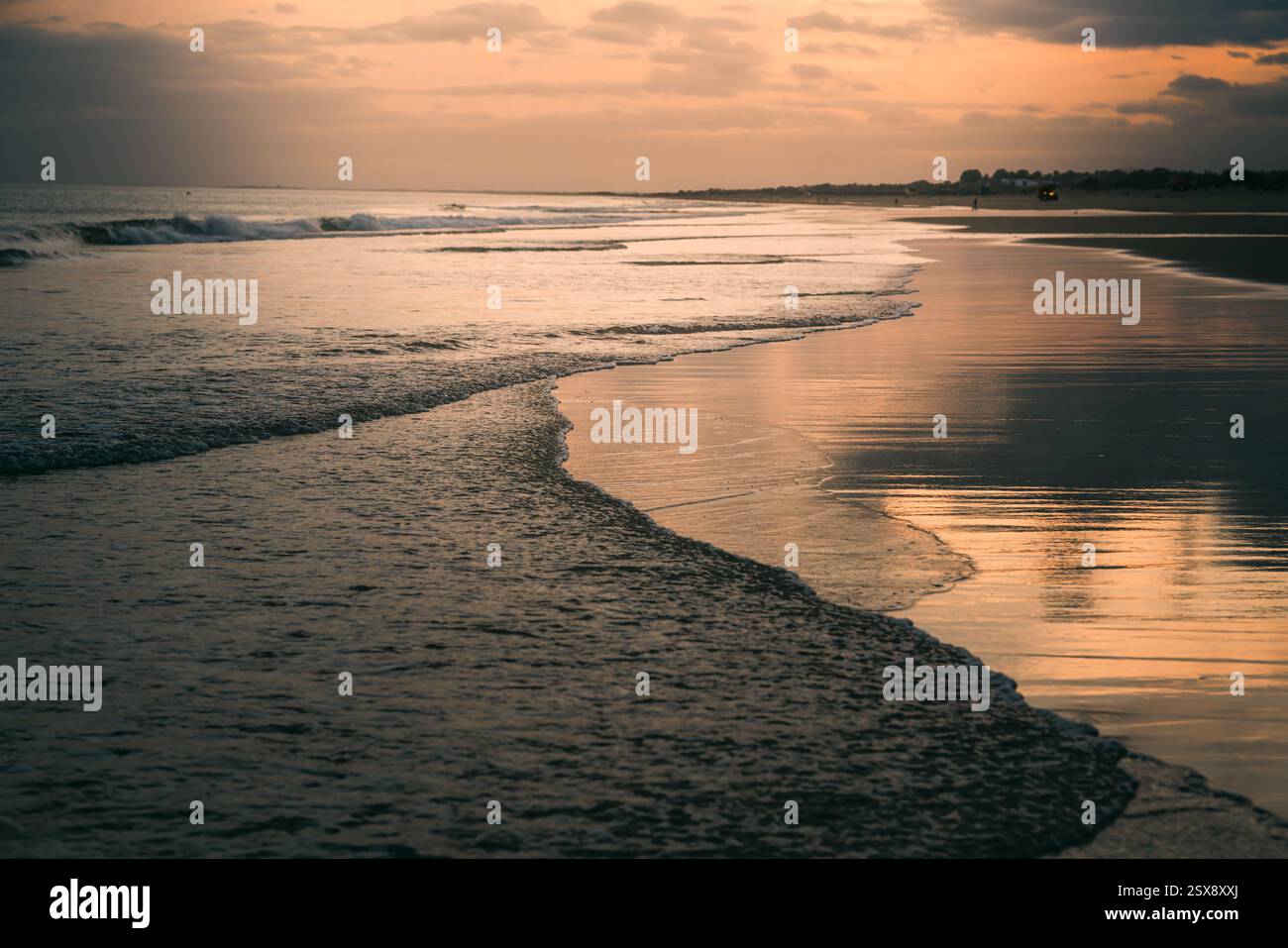Waves gently washing ashore under a dramatic sunset sky with clouds ...