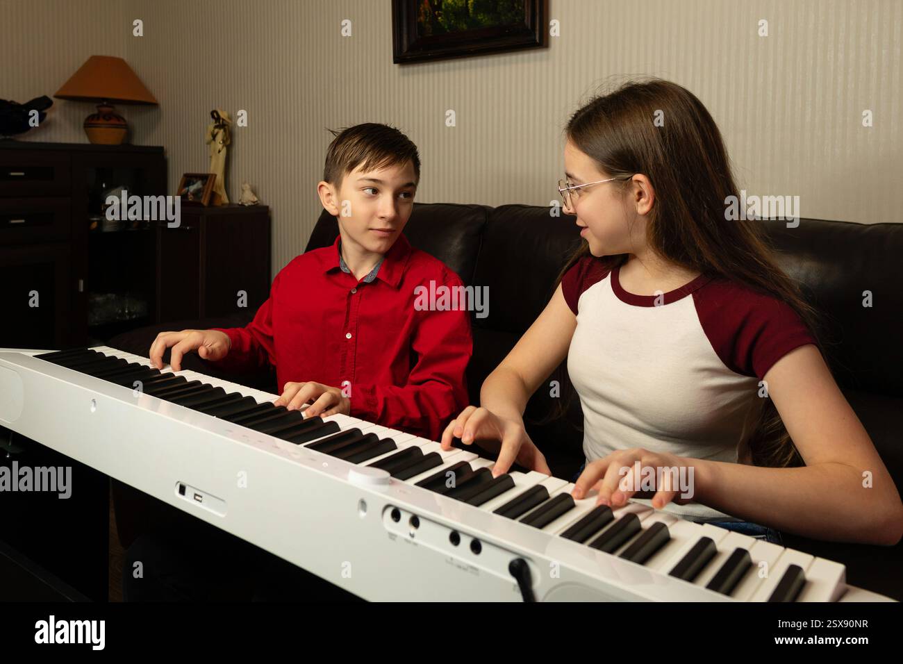 Two children playing the piano together, looking at each other ...