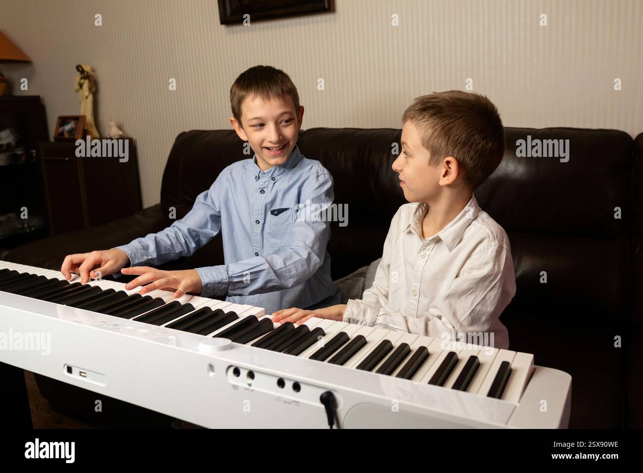 Two boys playing the keyboard and smiling. Practicing piano at home ...