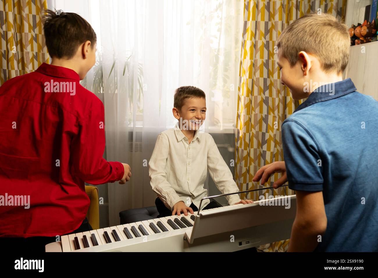 Smiling boy playing the piano while two friends watch. Practicing piano ...