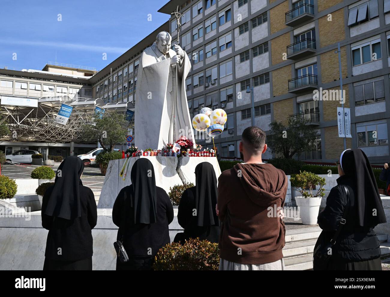 People pray near the statue of John Paul II outside the Gemelli ...