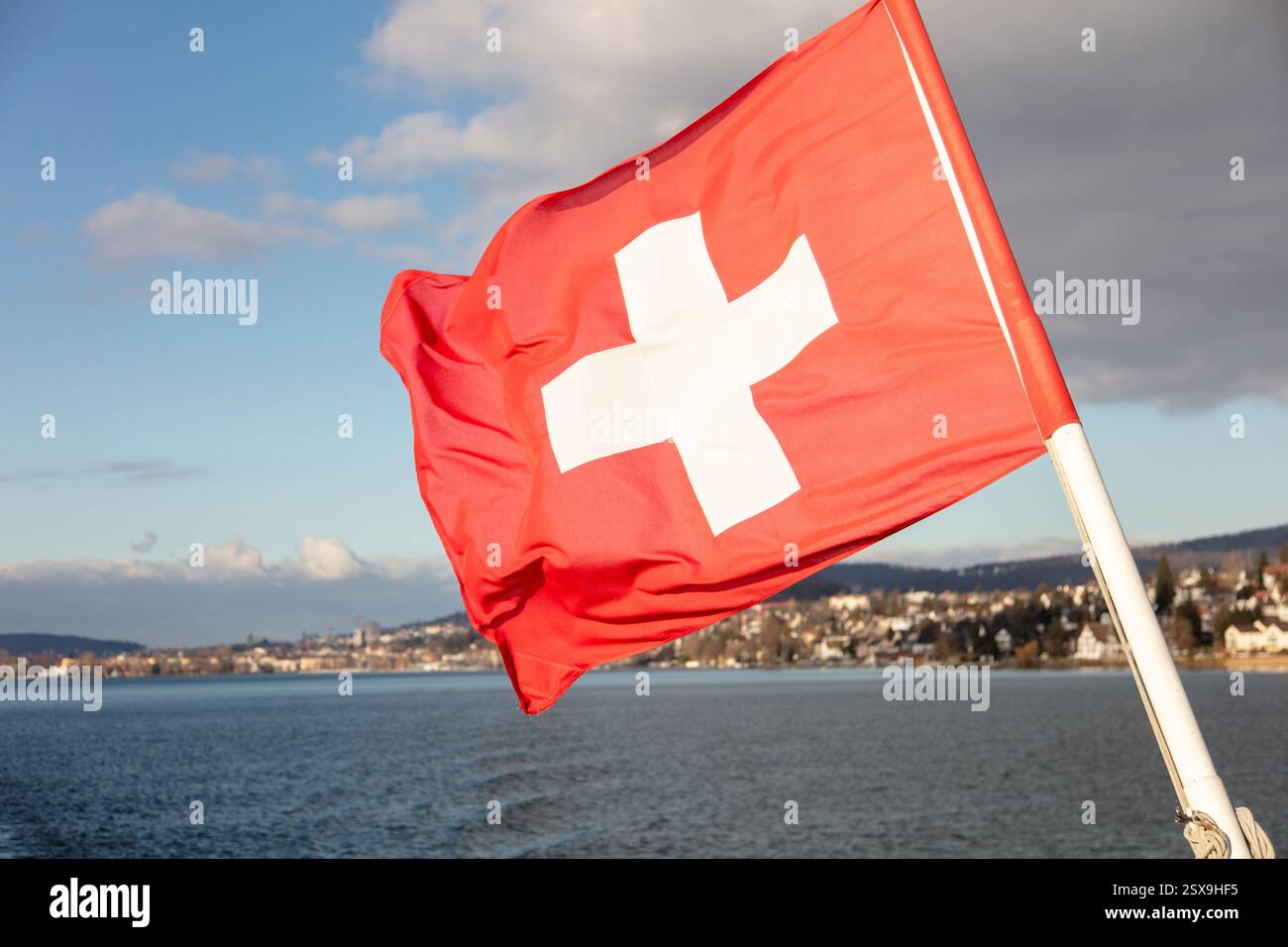 Swiss flag waving in the wind mounted on a ferry, Lake coast with ...