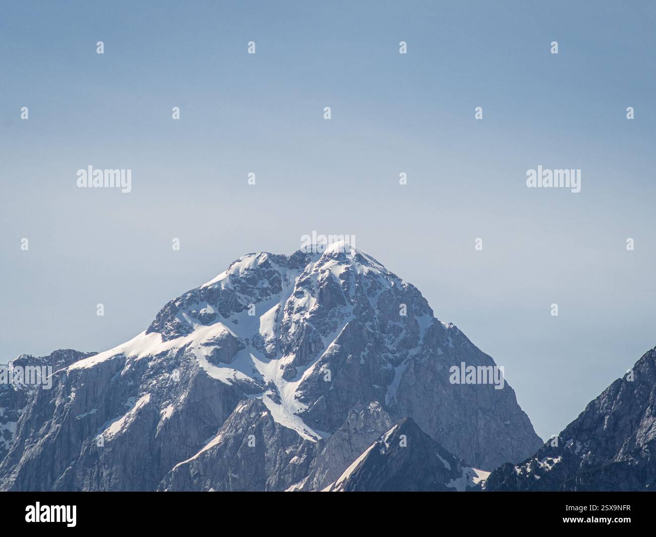 A majestic snow-capped mountain peak rises against a clear blue sky ...