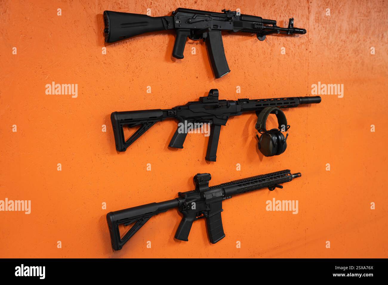 Modern guns in a shooting range on an orange wall. Rifles and carbines ...