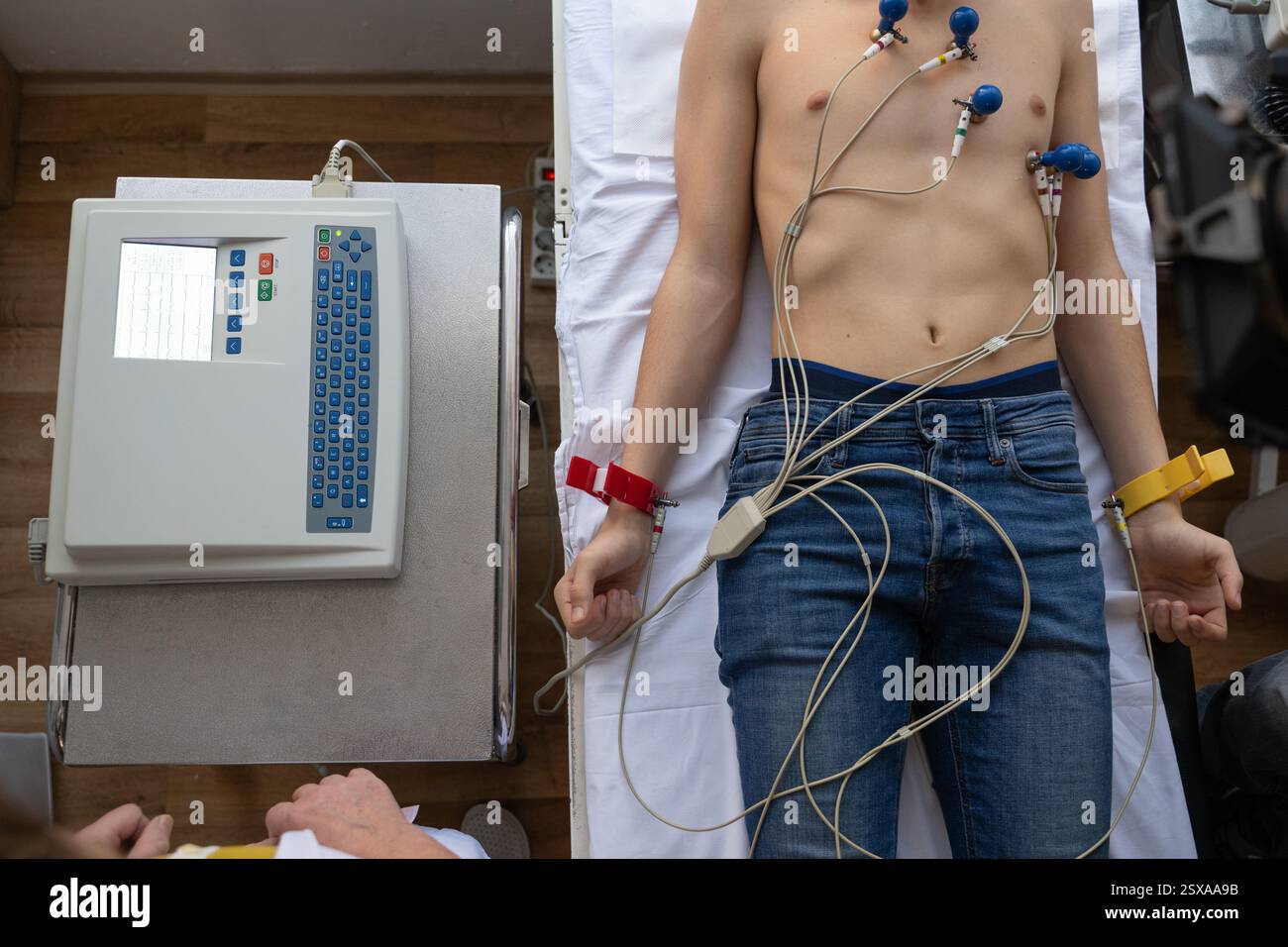 A female doctor performs an ECG on a young man in a hospital room ...