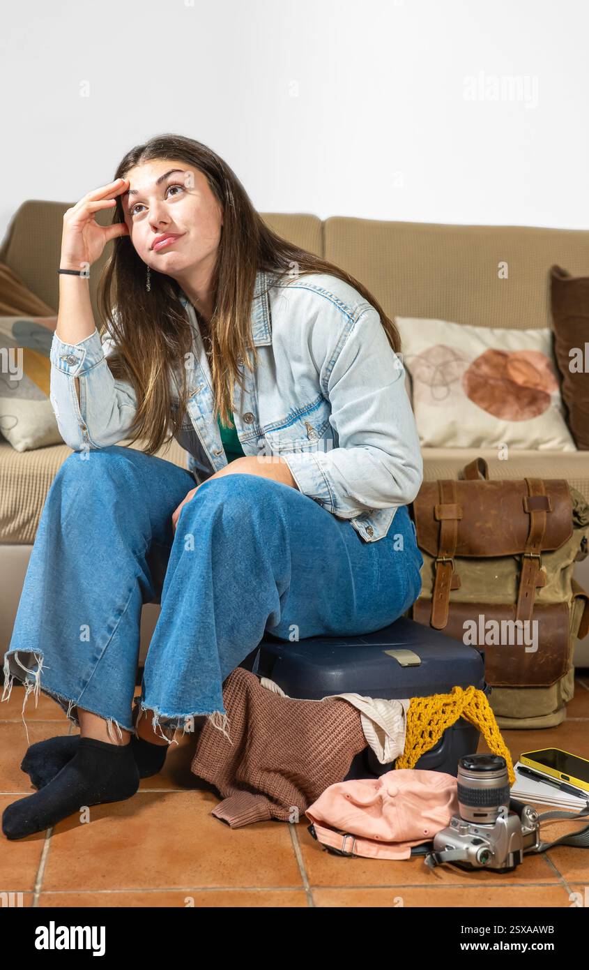 Traveler sitting on her suitcase with frustrated expression, clothes ...