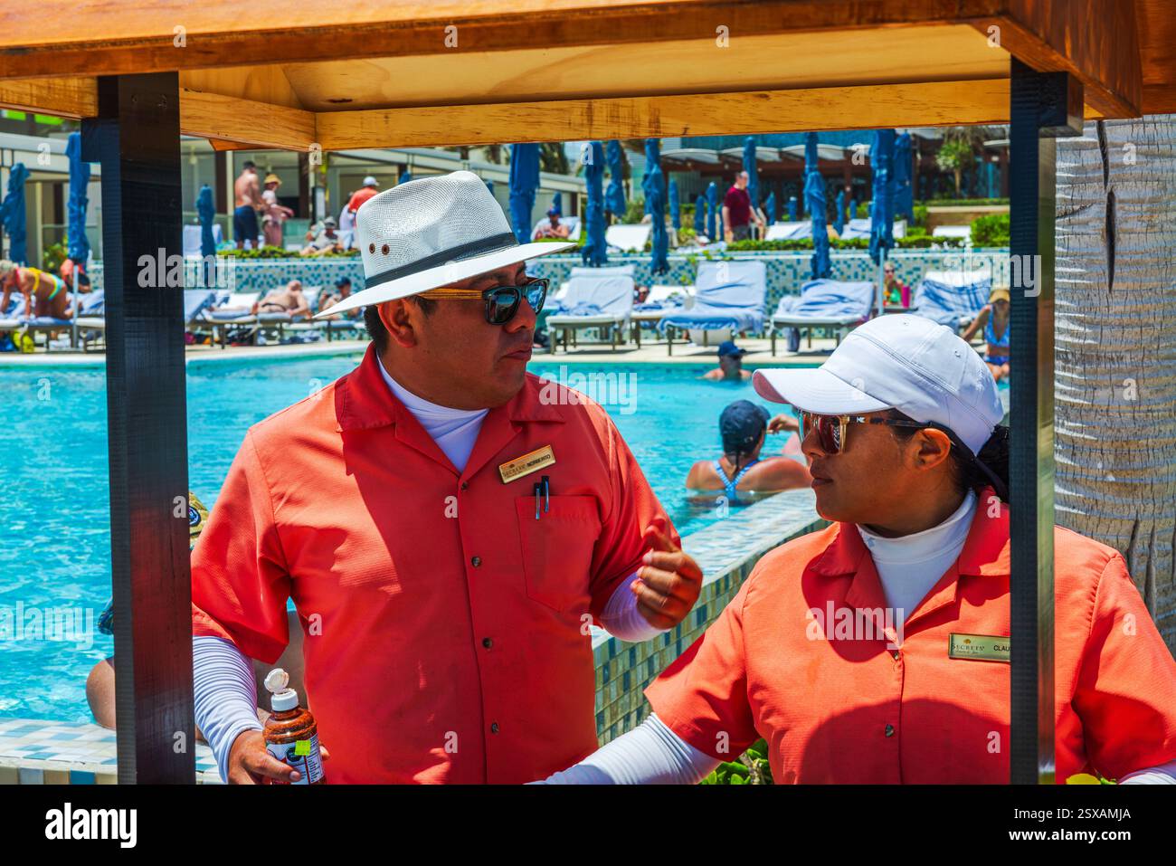 Two resort staff members in orange uniforms and hats talking near ...