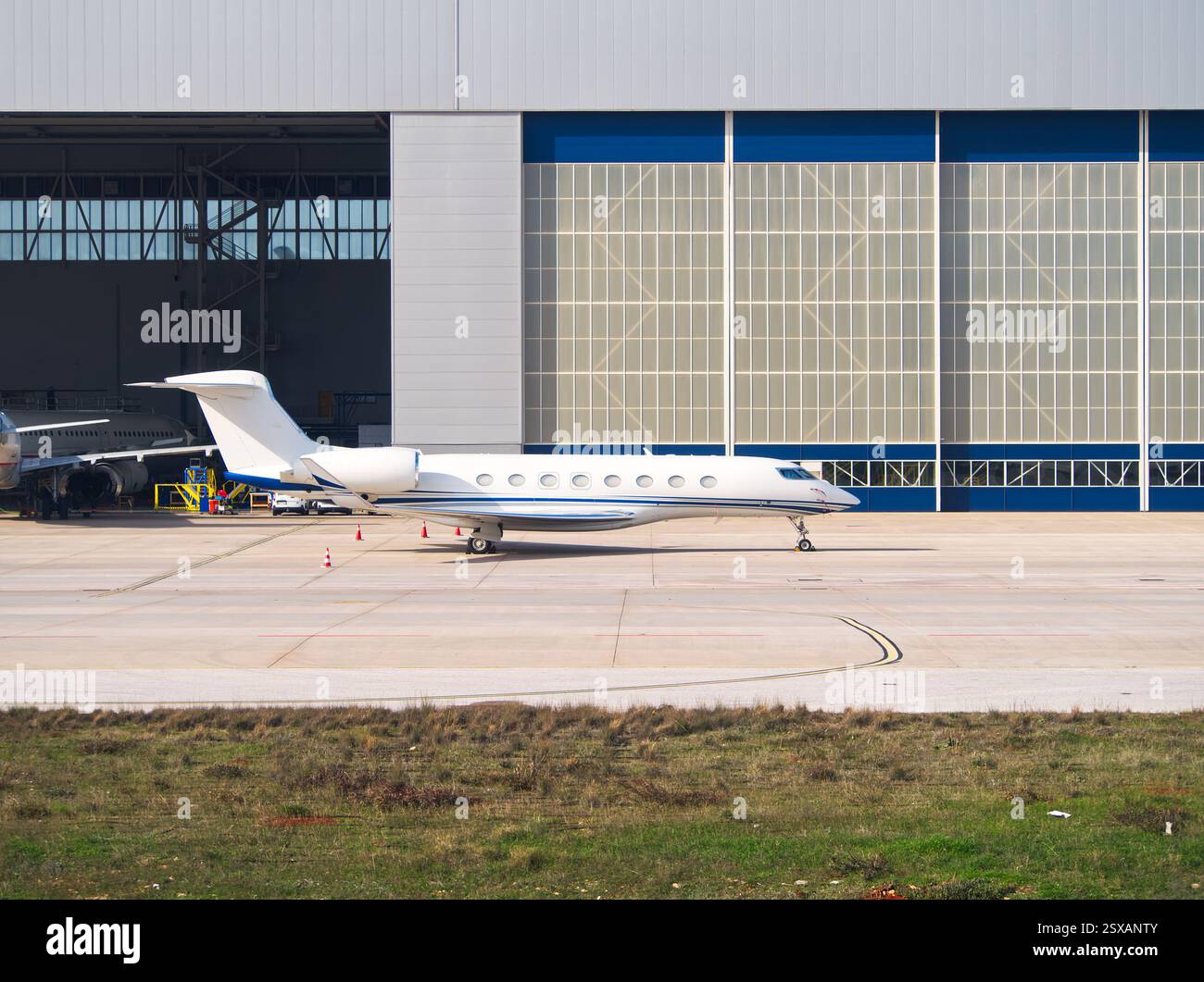 A sleek white private jet on tarmac near a large hangar with blue and ...